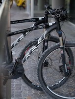 Uma bicicleta com a marca "REZ" e autocolantes "ROCK SHOX" nos pneus, estacionada ao lado de uma estrutura de metal com a placa "LAKEFRONT HOTEL MIRAGE".