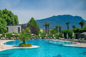 Piscina com espreguiçadeiras e guarda-sóis, cercada por vegetação e uma montanha ao fundo.