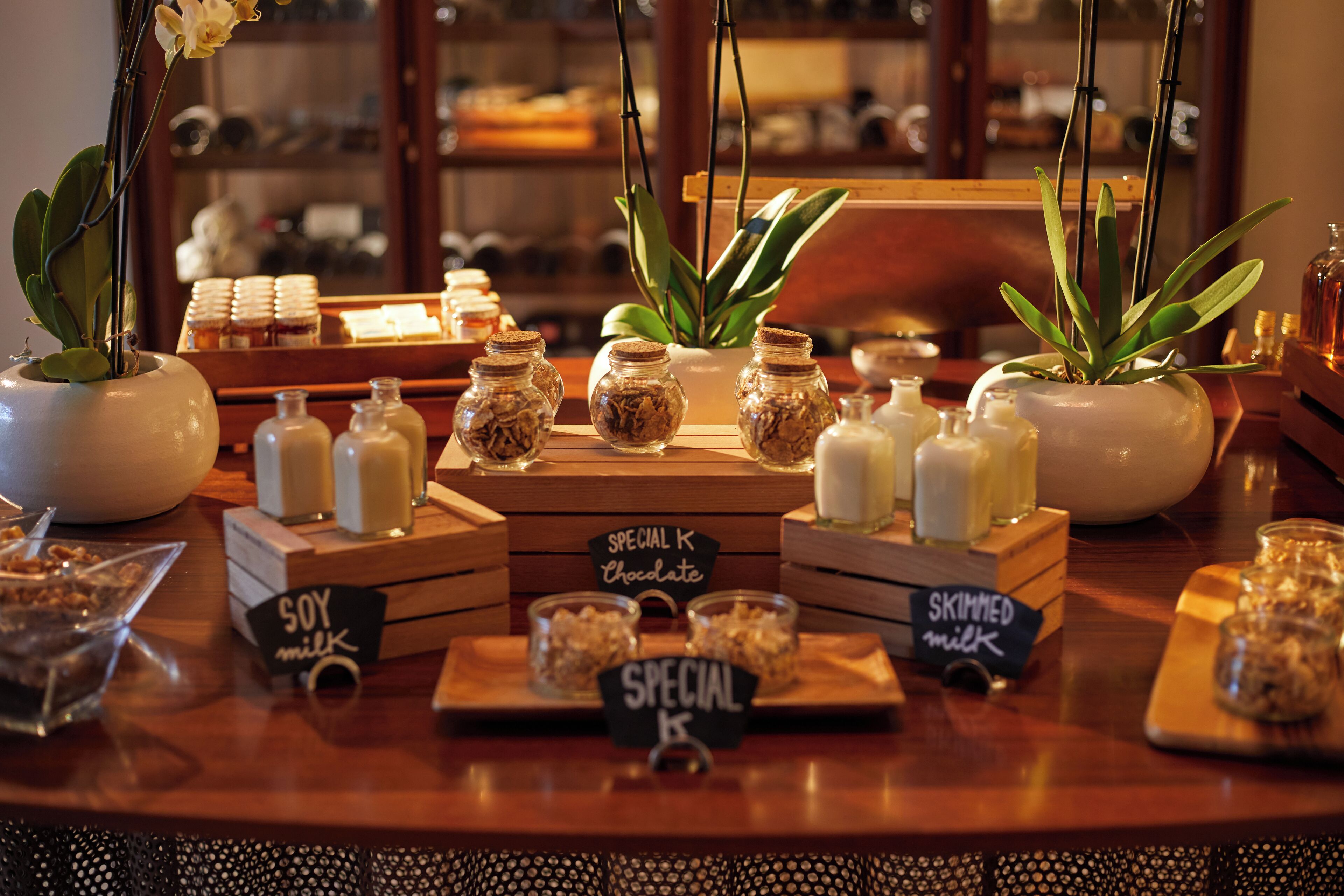 Uma área de bar com diversas opções de comida e bebida, incluindo potes de petiscos, garrafas de leite e um aviso sobre chocolate especial.