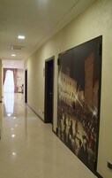 Um corredor de hotel com piso lustroso, portas e um grande mural na parede retratando uma cena histórica.