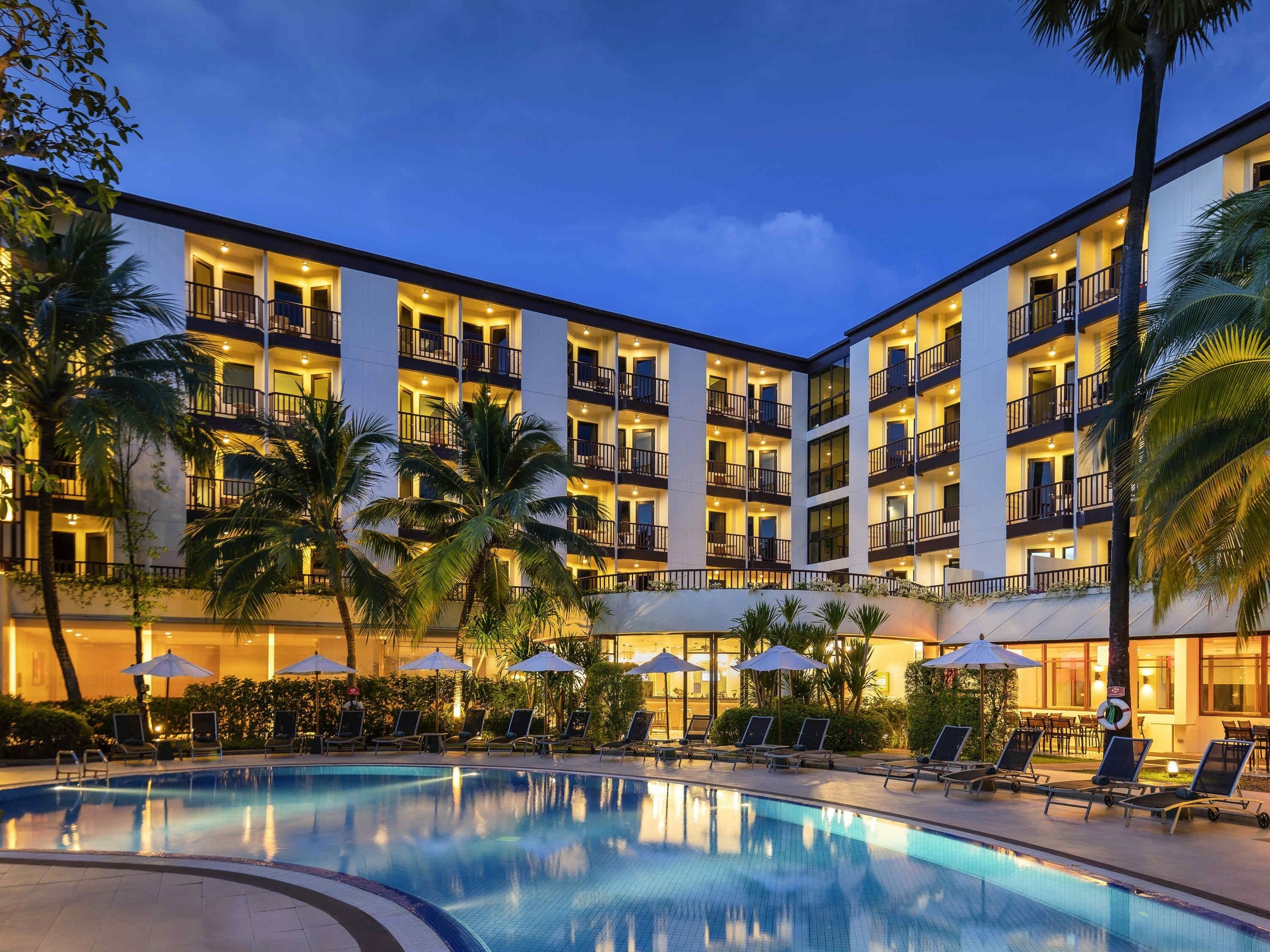 Um hotel com piscina, várias varandas e palmeiras.