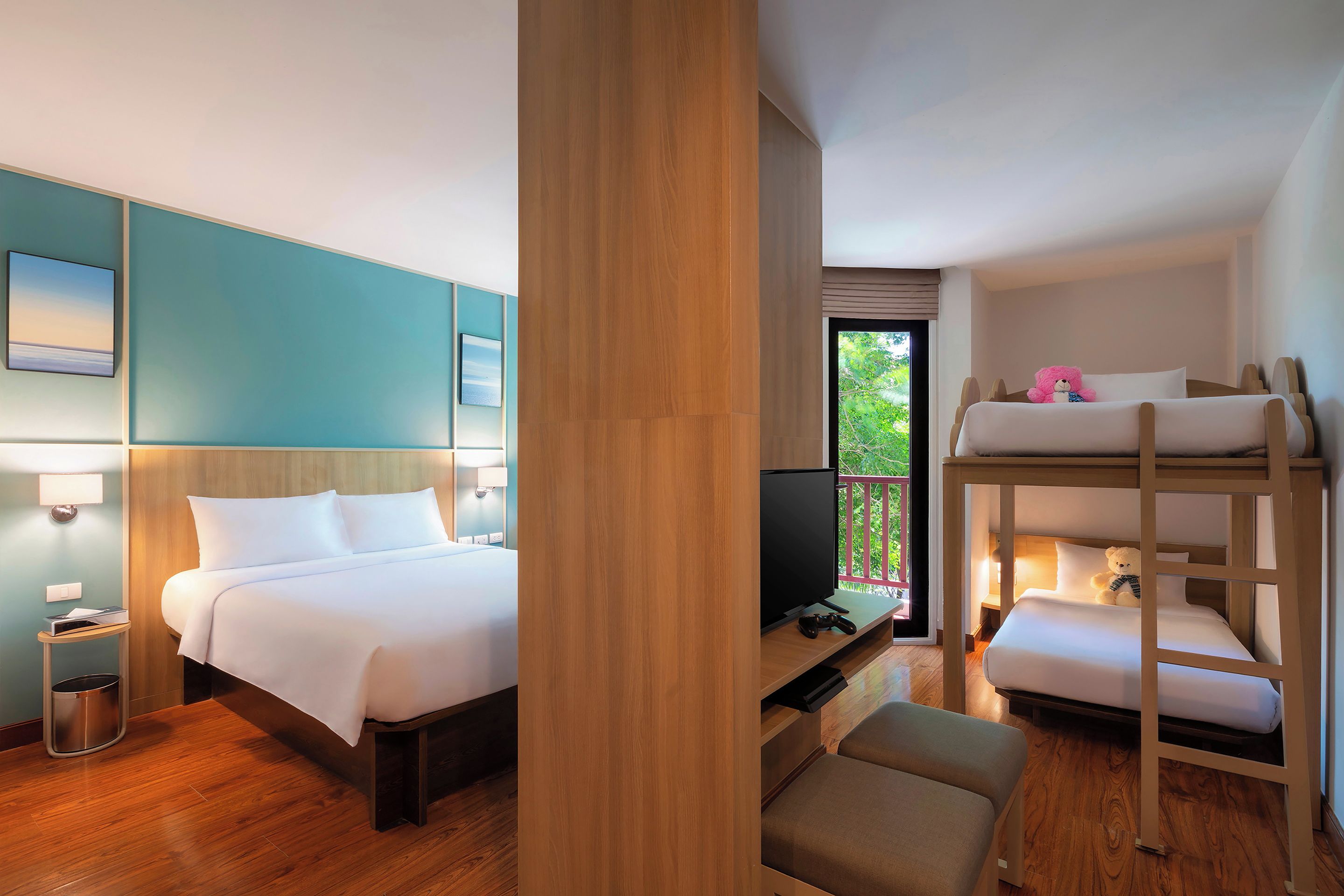 Quarto de hotel com beliche, uma cama de solteiro, escrivaninha com computador e janela com vista para o verde.