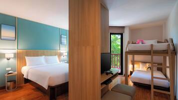 Quarto de hotel com beliche, uma cama de solteiro, escrivaninha com computador e janela com vista para o verde.