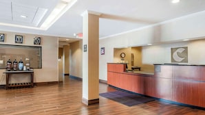 Uma área de recepção de hotel com piso de madeira, balcão de atendimento, relógio e prêmios emoldurados na parede.