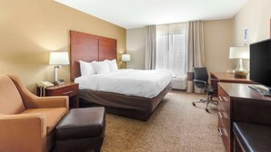 Quarto de hotel com uma cama grande, uma mesa com computador, uma cadeira, televisão e telefone.