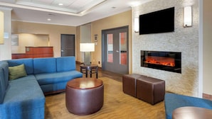 Um lobby moderno de hotel com um sofá azul, uma mesa de centro redonda de madeira e uma lareira.