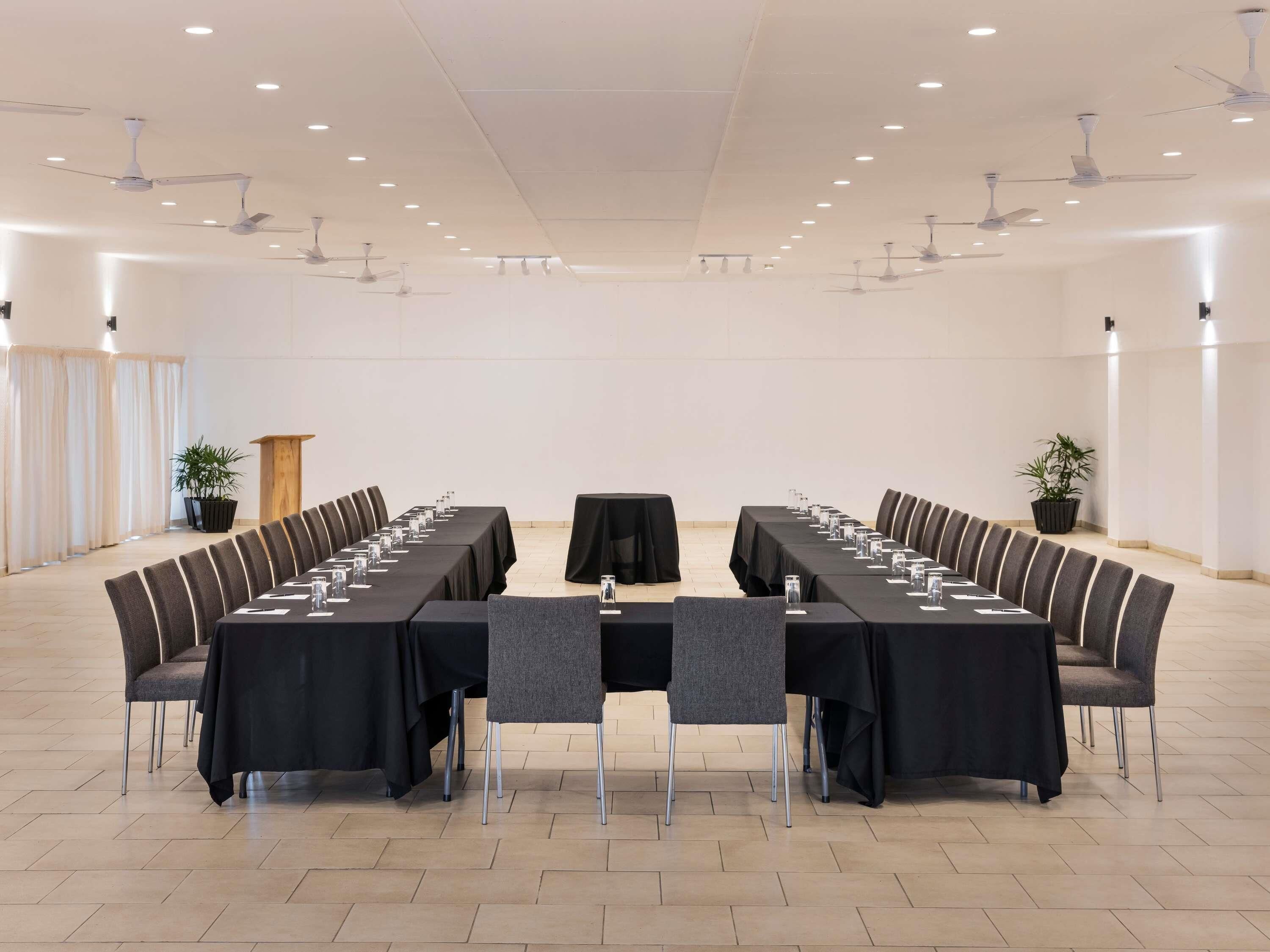 Uma sala de conferência com uma mesa comprida, cadeiras, ventiladores de teto e iluminação embutida.