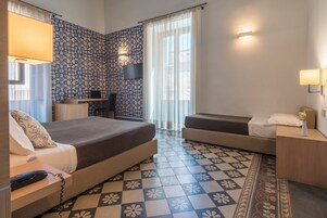 Quarto de hotel com uma cama, escrivaninha, cadeira, luminária e televisão.