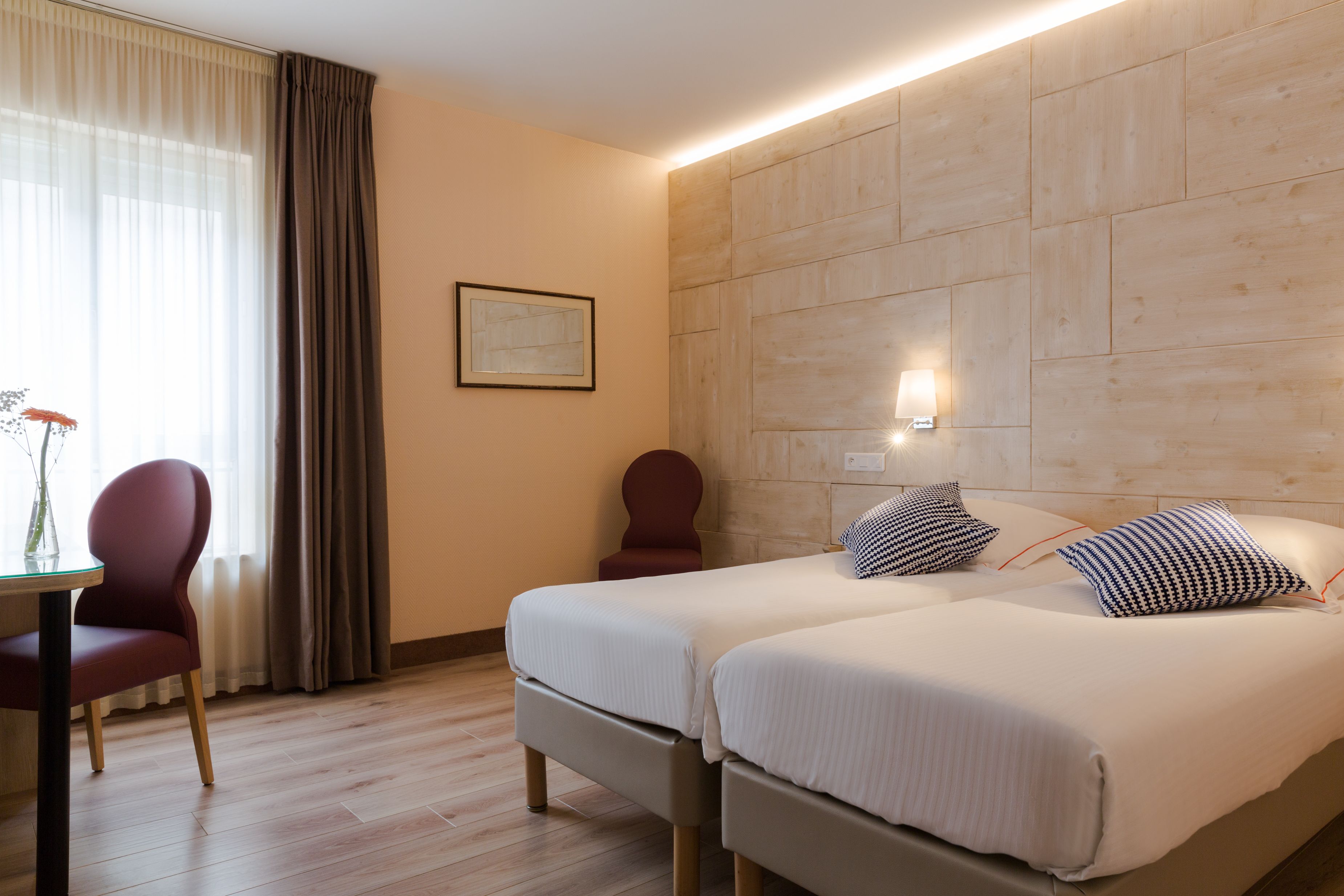 Quarto de hotel com duas camas, uma escrivaninha, uma cadeira e uma janela com cortinas.