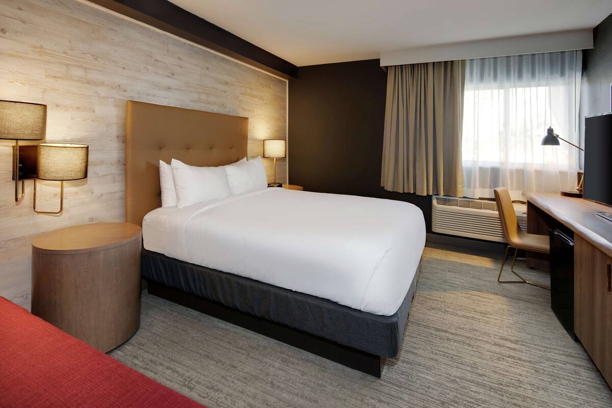 Quarto de hotel moderno com uma cama grande, duas luminárias de cabeceira, uma escrivaninha e uma televisão.