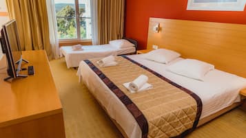 Quarto de hotel com duas camas, uma escrivaninha com computador e telefone, e uma janela com cortinas.