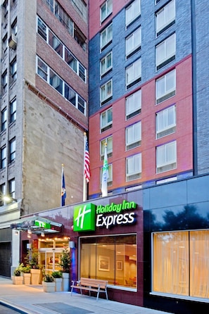 Edifício Holiday Inn Express com fachada de tijolos, grandes janelas e uma bandeira americana visível.