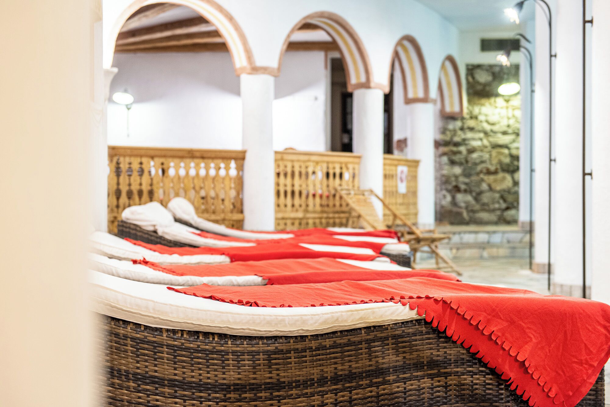 Um quarto de spa com vários espreguiçadeiras, parede de pedra e arcos de madeira.