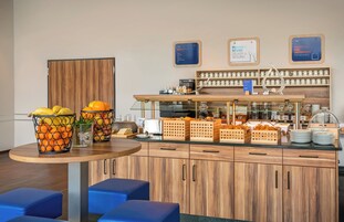Balcão de café da manhã com cestas de frutas, uma máquina de café e uma variedade de canecas.
