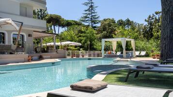 Piscina com espreguiçadeiras e guarda-sóis, cercada por vegetação e um edifício moderno.