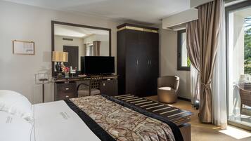Quarto de hotel com uma cama, uma escrivaninha com televisão, guarda-roupa, uma cadeira e uma janela grande com cortinas.