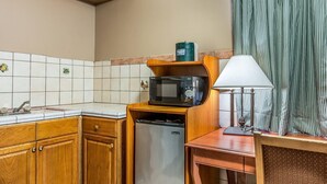 Uma cozinha compacta com armários de madeira, micro-ondas, frigorífico pequeno, pia e uma mesa com candeeiro.