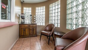 Quarto com teto curvo, um armário de madeira, uma máquina de café, duas poltronas de couro e janelas amplas com padrão quadriculado.