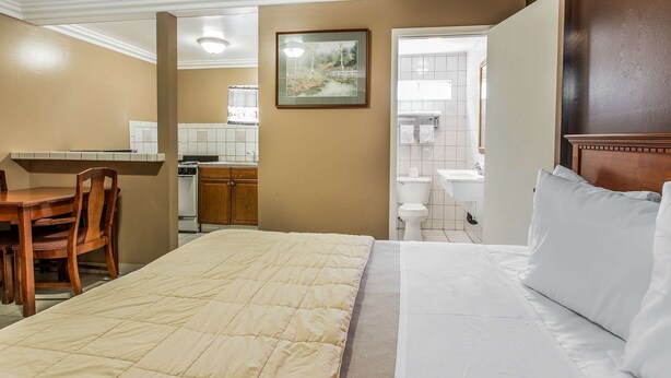 Quarto de hotel com cama, escrivaninha e vista para a cozinha e o banheiro.