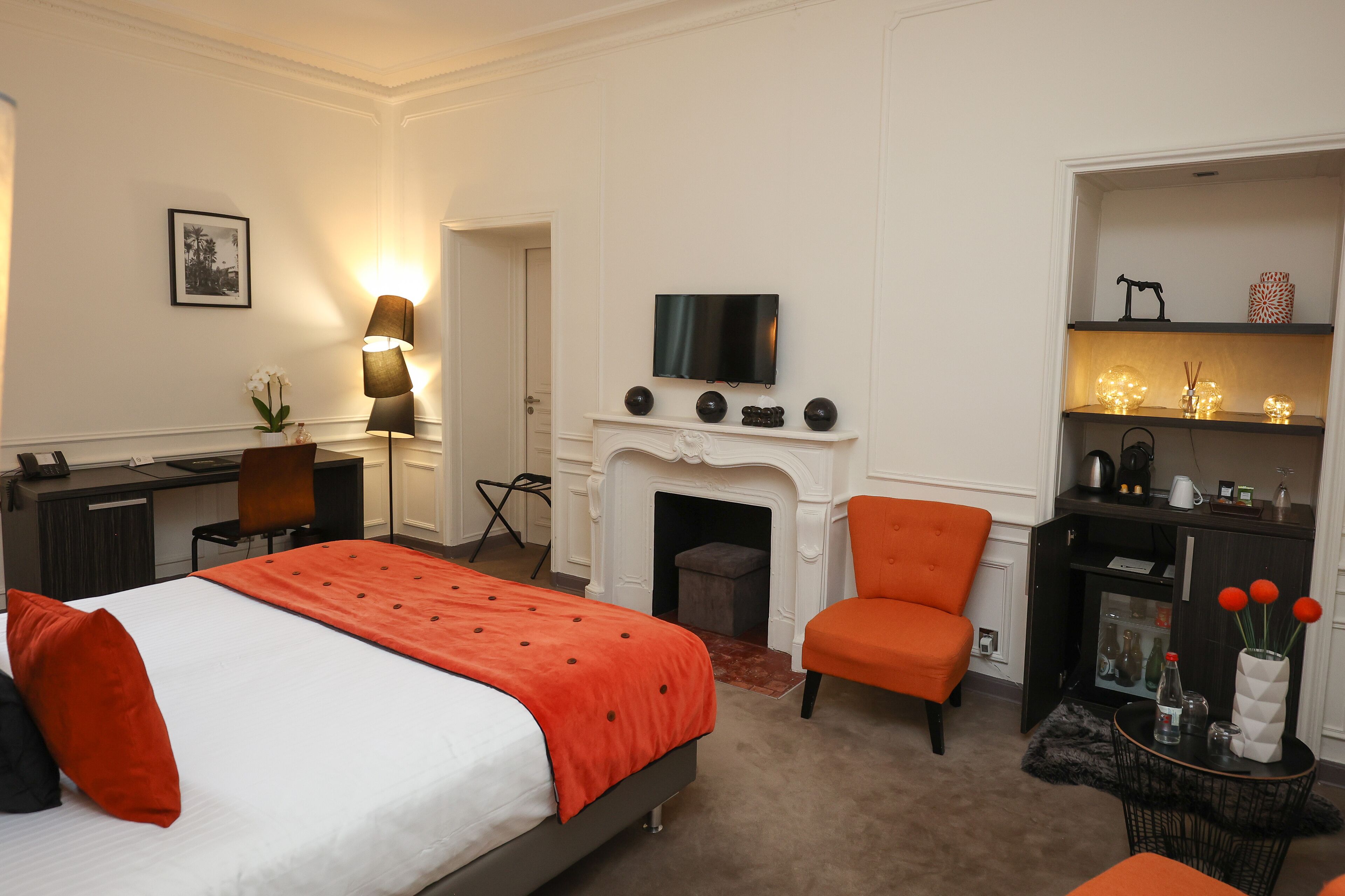 Quarto de hotel com cama, escrivaninha, poltrona, lareira e televisão.