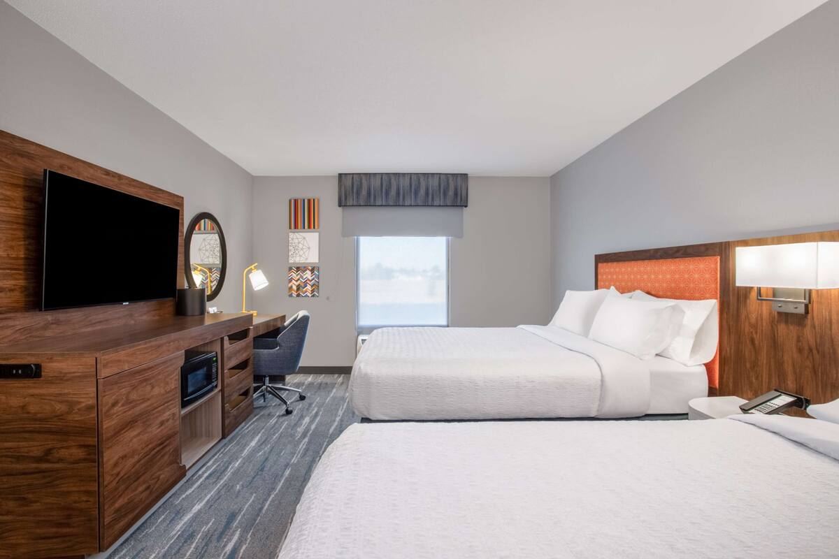 Quarto de hotel com uma cama grande, uma escrivaninha com televisão de tela plana, micro-ondas e uma cadeira.