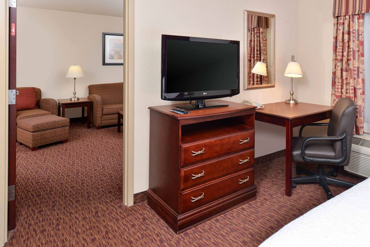Quarto de hotel com televisão, escrivaninha, cadeira, cômoda e cama.