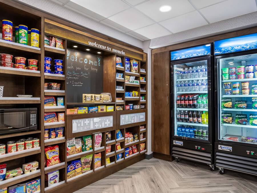 Quiosque de lanches e bebidas com prateleiras repletas de diversos petiscos e bebidas, e dois dispensadores refrigerados.