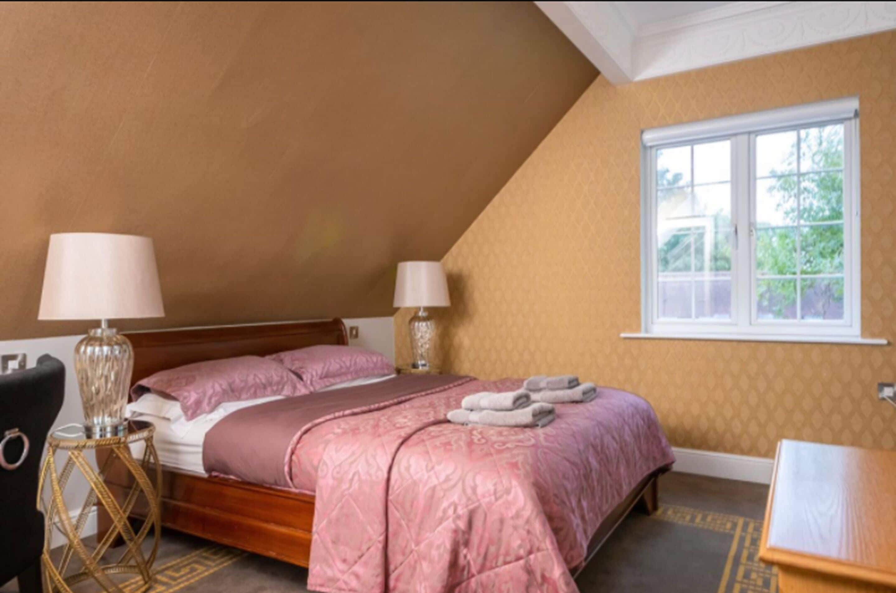 Quarto com cama, duas luminárias de cabeceira, janela e mesa de cabeceira de madeira.