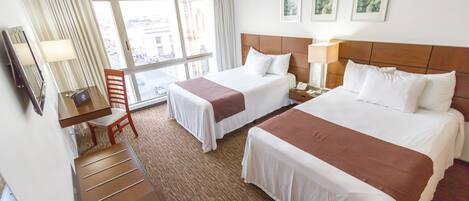 Quarto de hotel com duas camas, uma escrivaninha, uma cadeira, uma televisão e vista para a cidade.