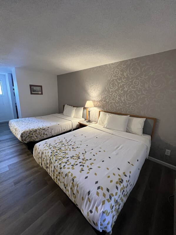 Quarto de hotel com duas camas, uma mesa de cabeceira, uma luminária e parede com padrão.
