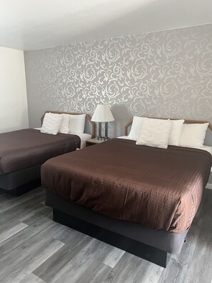 Quarto de hotel com duas camas, uma mesa de cabeceira com abajur e papel de parede estampado.