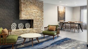 Uma sala de estar moderna com lareira de pedra, poltronas estofadas em verde, uma mesa de centro redonda e um espaço de jantar com cadeiras e mesa de madeira.