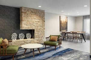 Uma sala de estar moderna com lareira de pedra, poltronas estofadas em verde, uma mesa de centro redonda e um espaço de jantar com cadeiras e mesa de madeira.