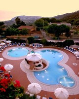 Uma área de piscina com várias piscinas circulares, espreguiçadeiras, guarda-sóis e vista para a paisagem ao redor.