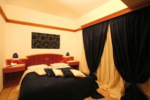 Quarto de hotel com cama, duas mesas de cabeceira, luminária, obra de arte na parede e cortinas preto e branco.