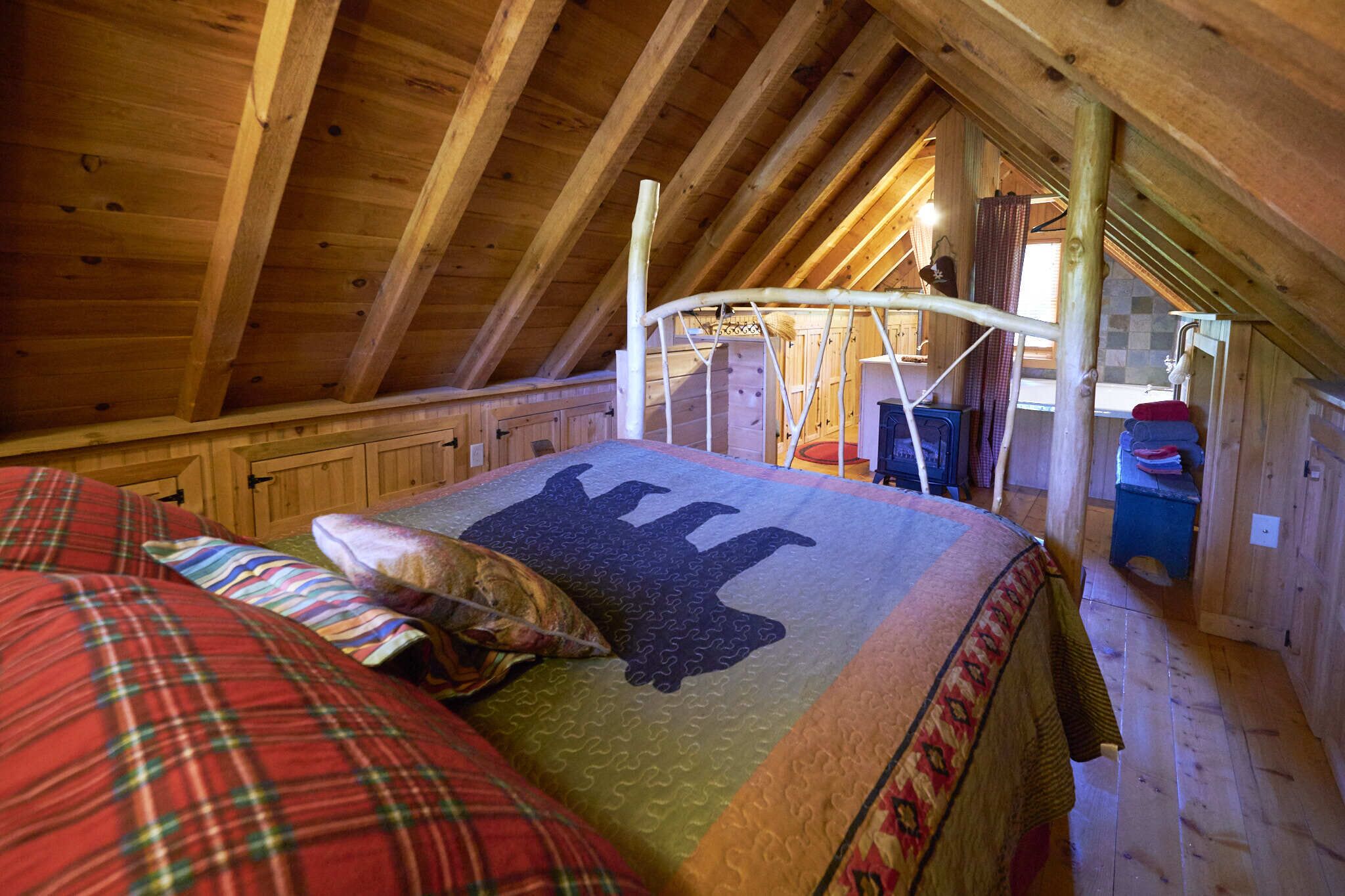 Um quarto de sótão acolhedor, com teto de madeira, uma cama com colcha estampada e uma janela com cortinas.