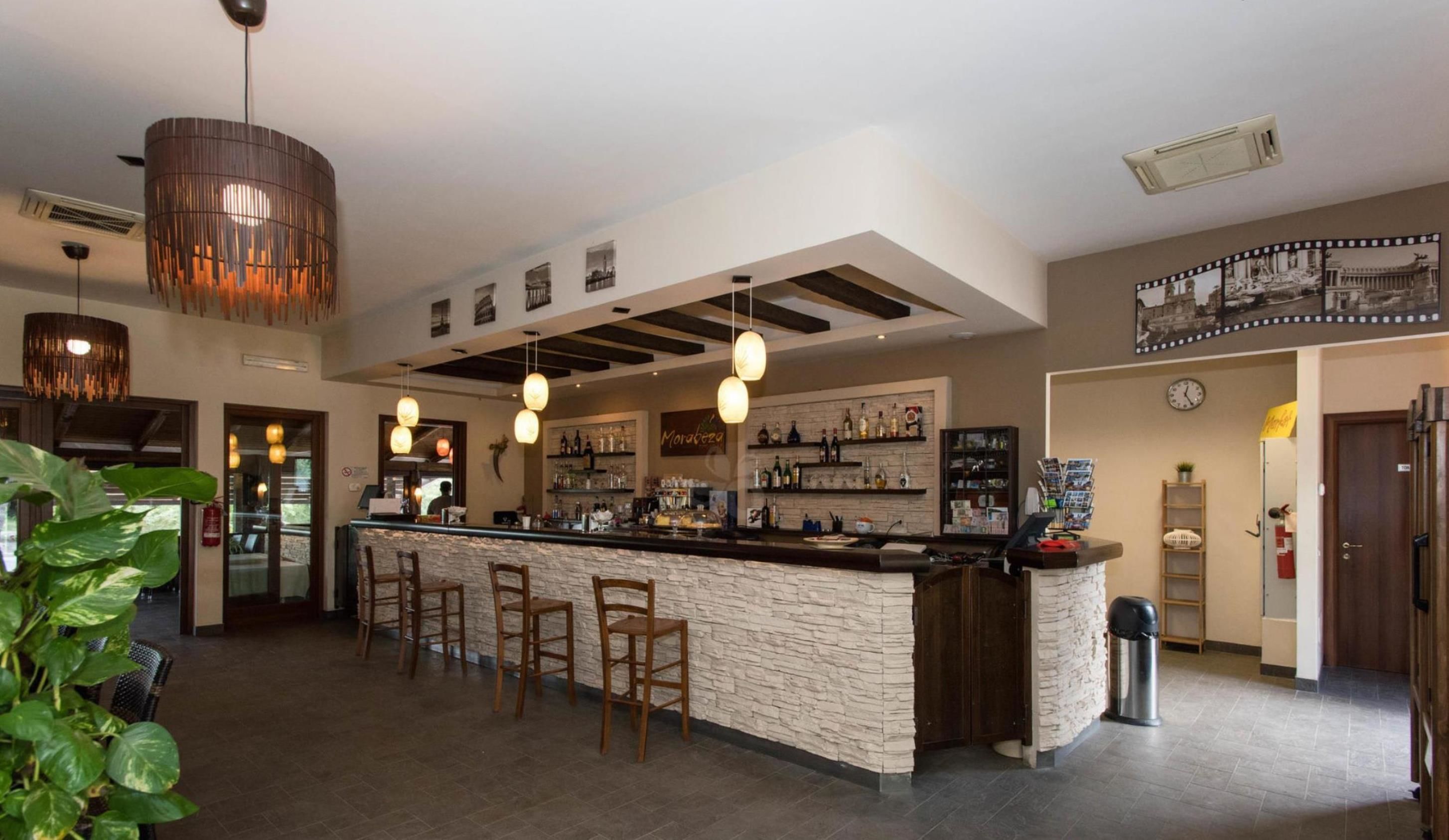 Uma área de bar com balcão de pedra, luminárias pendentes e diversas garrafas em prateleiras.