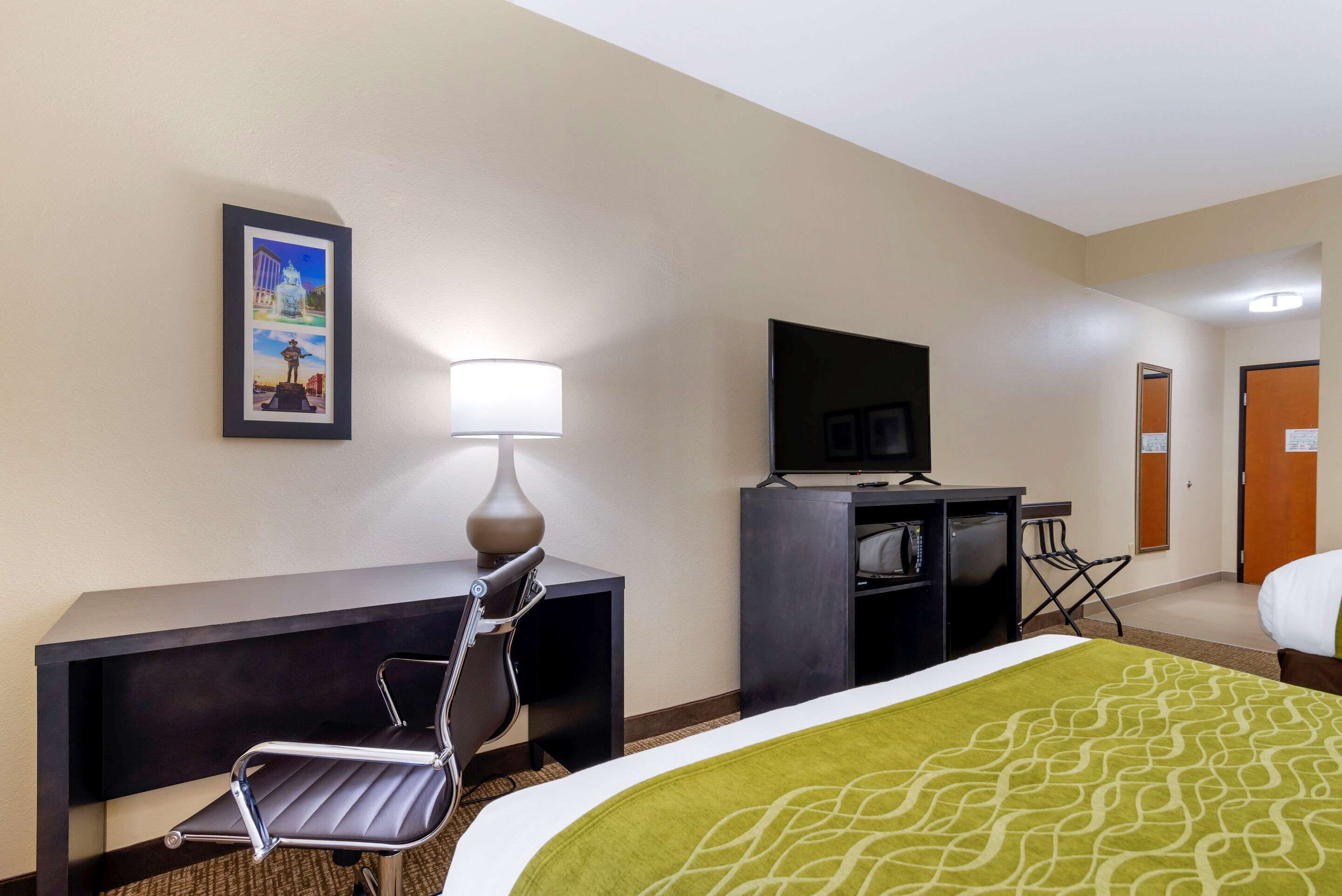 Quarto de hotel com cama, escrivaninha, cadeira, televisão e abajur.