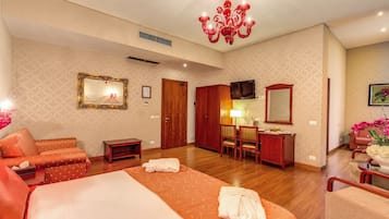 Quarto de hotel com uma cama grande, um espaço de estar com sofá, uma escrivaninha com cadeira, televisão e espelho.