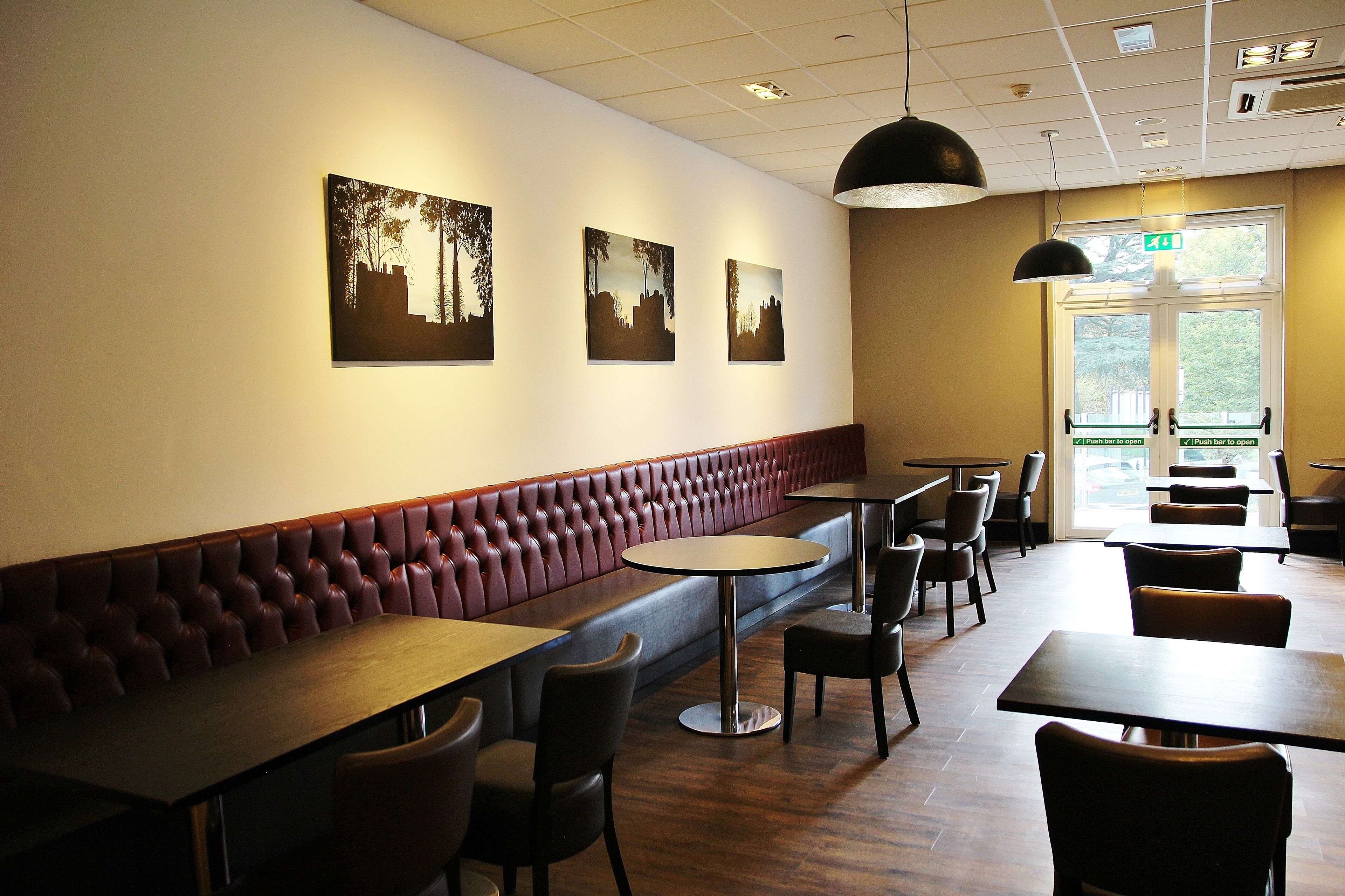Interior de restaurante com um amplo assento em camarote, mesas individuais e cadeiras.