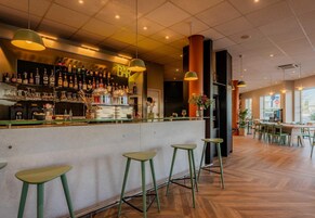 Uma área de bar com banquetas, balcão e diversas garrafas e copos.