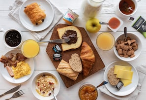 Uma mesa de café da manhã com diversos alimentos, incluindo torradas, ovos, bacon e cereais.
