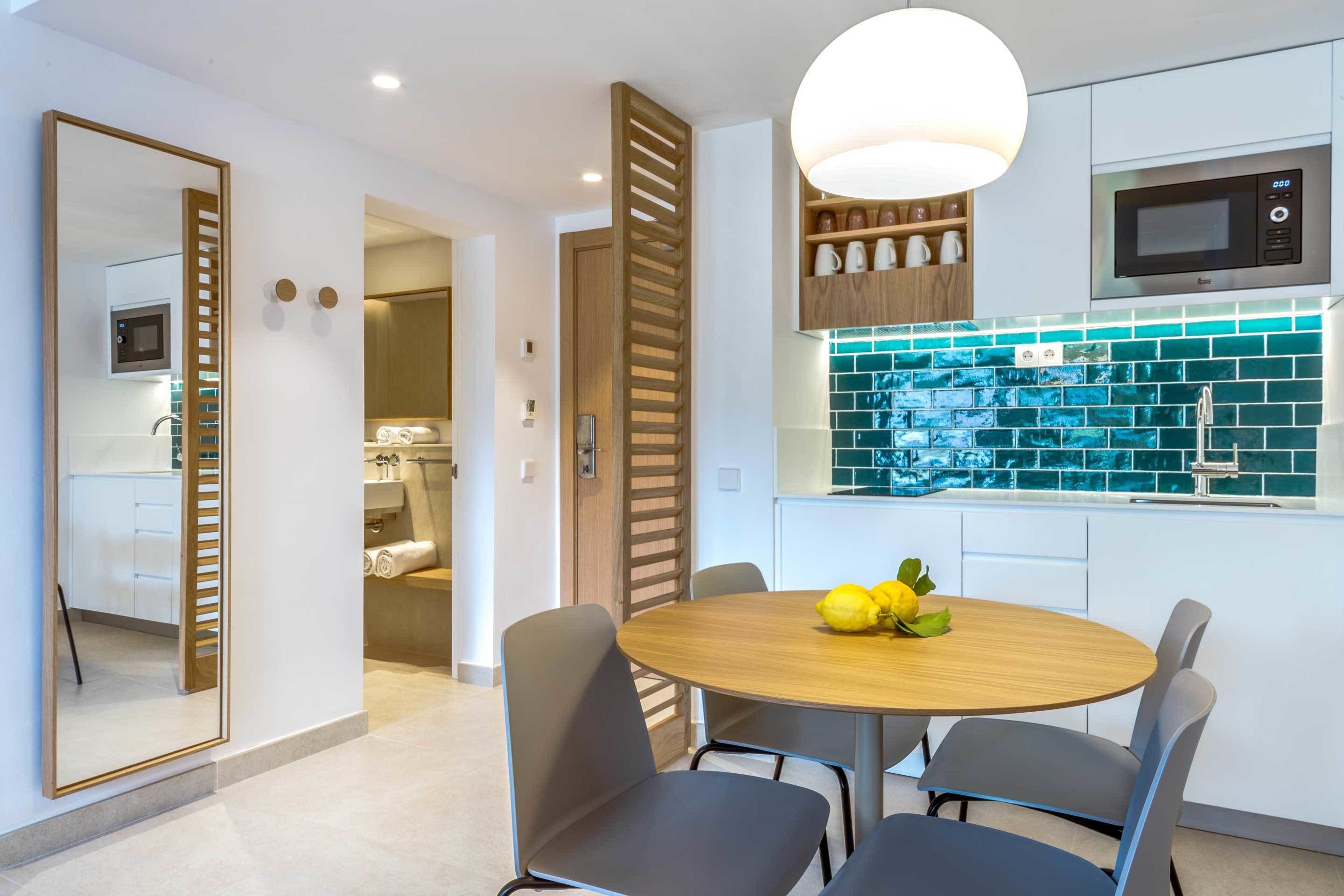 Cozinha moderna com mesa redonda de madeira, cadeiras cinzas e micro-ondas acima.