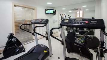 Uma academia com esteiras, elípticos e uma tela de televisão.
