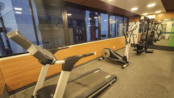 Academia com equipamentos de cardio, painéis de madeira e janelas amplas.