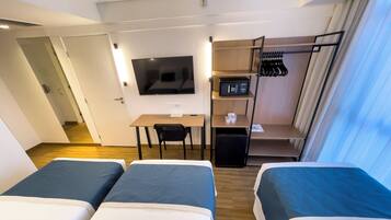 Quarto de hotel com duas camas, uma escrivaninha, televisão, guarda-roupa e uma pequena cozinha equipada.