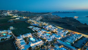 Vista aérea de uma vila costeira com edifícios brancos, piscina e vista para o mar.