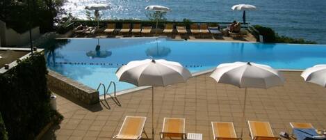 Área da piscina com espreguiçadeiras e guarda-sóis, com vista para o mar.
