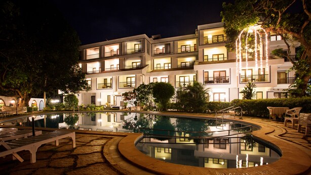 Um hotel com piscina, espreguiçadeiras e fachada bem iluminada.
