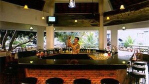 Uma área de bar com balcão, banquetas e uma tela de televisão.